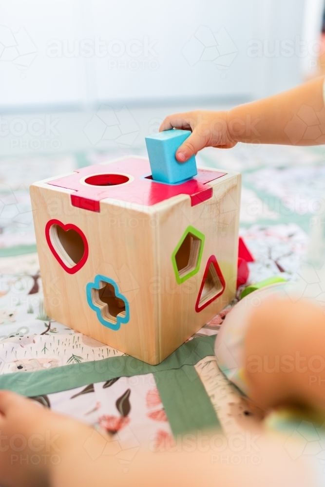 Image of Toddler posting coloured shapes into wooden shape sorter box ...