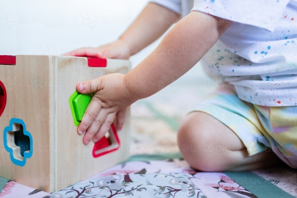 Image of Toddler posting coloured shapes into wooden shape sorter box ...