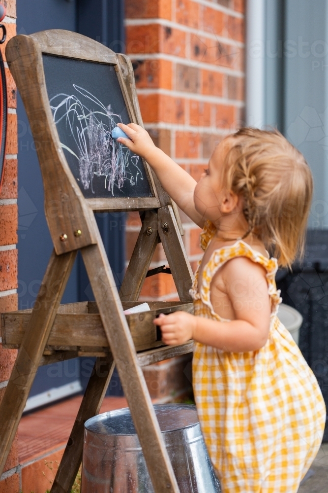 Image of Toddler reaching up to draw on chalk board outside - Austockphoto