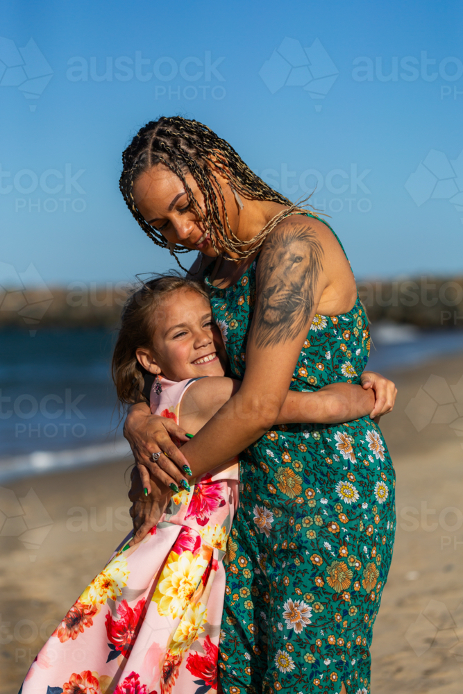Image of Torres Strait Islander girl and mother hug on beach together in Australian sunshine ...