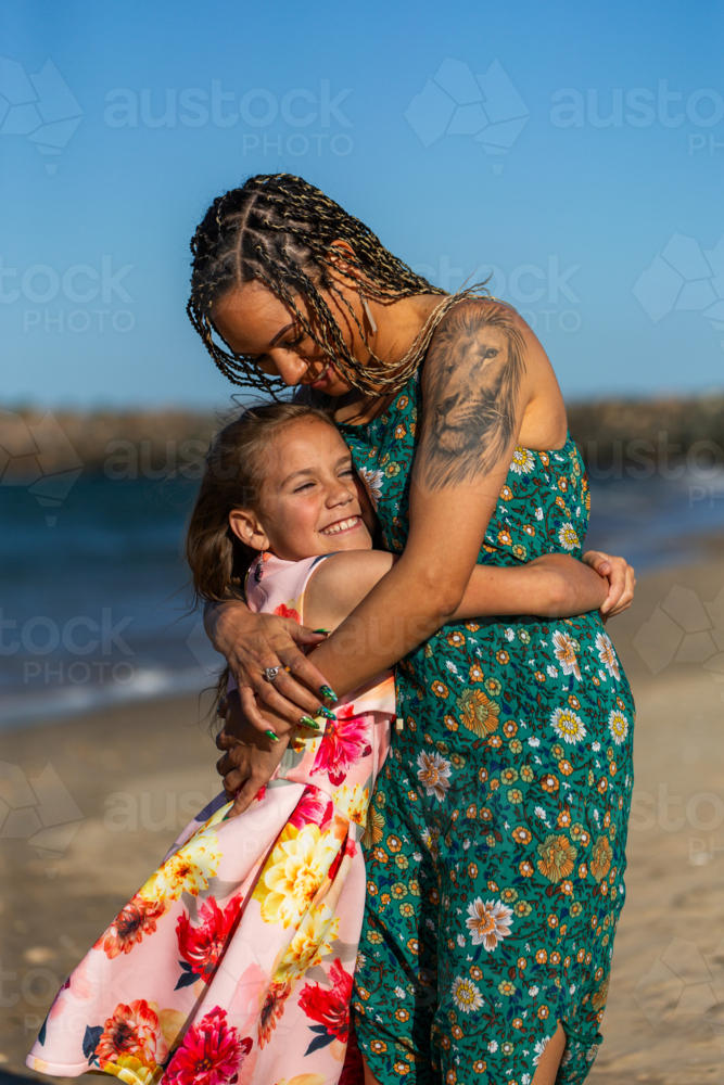 Image of Torres Strait Islander girl and mother hug on beach together in Australian sunshine ...
