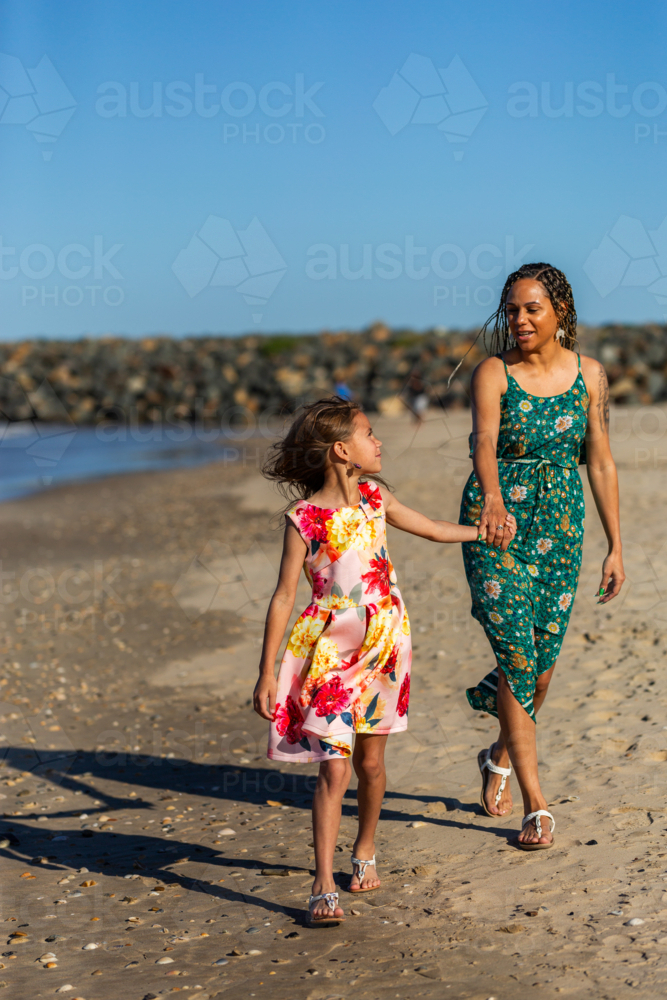 Image of Torres Strait Islander girl and mother walking on beach shoreline together in ...