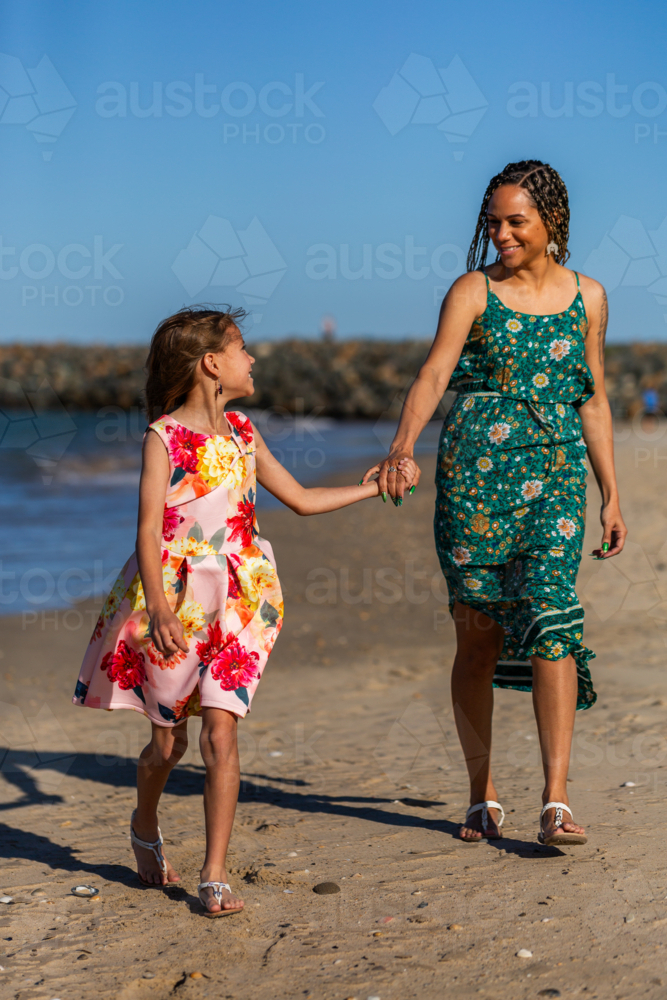 Image of Torres Strait Islander girl and mother walking on beach shoreline together in ...