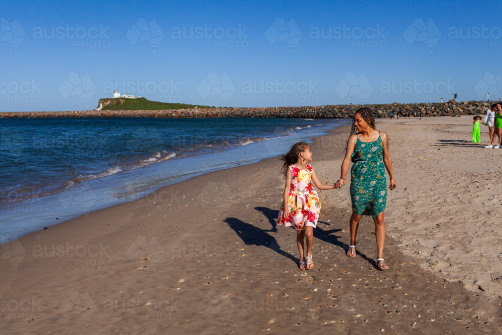 Image of Torres Strait Islander girl and mother walking on beach shoreline together in ...