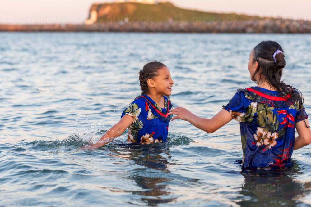 Image of Torres Strait Islander girls in traditional floral dresses playing and splashing in ...