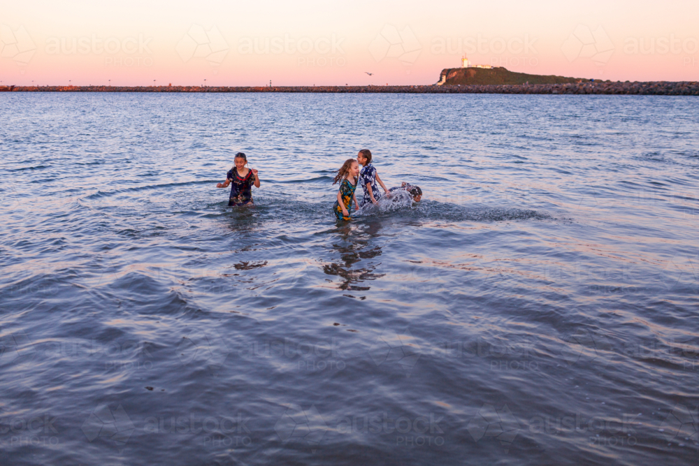 Image of Torres Strait Islander girls in traditional floral dresses playing and splashing in ...