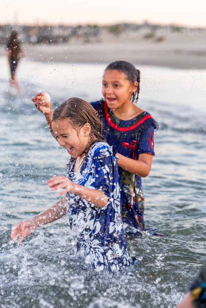 Image of Torres Strait Islander girls in traditional floral dresses playing and splashing in ...