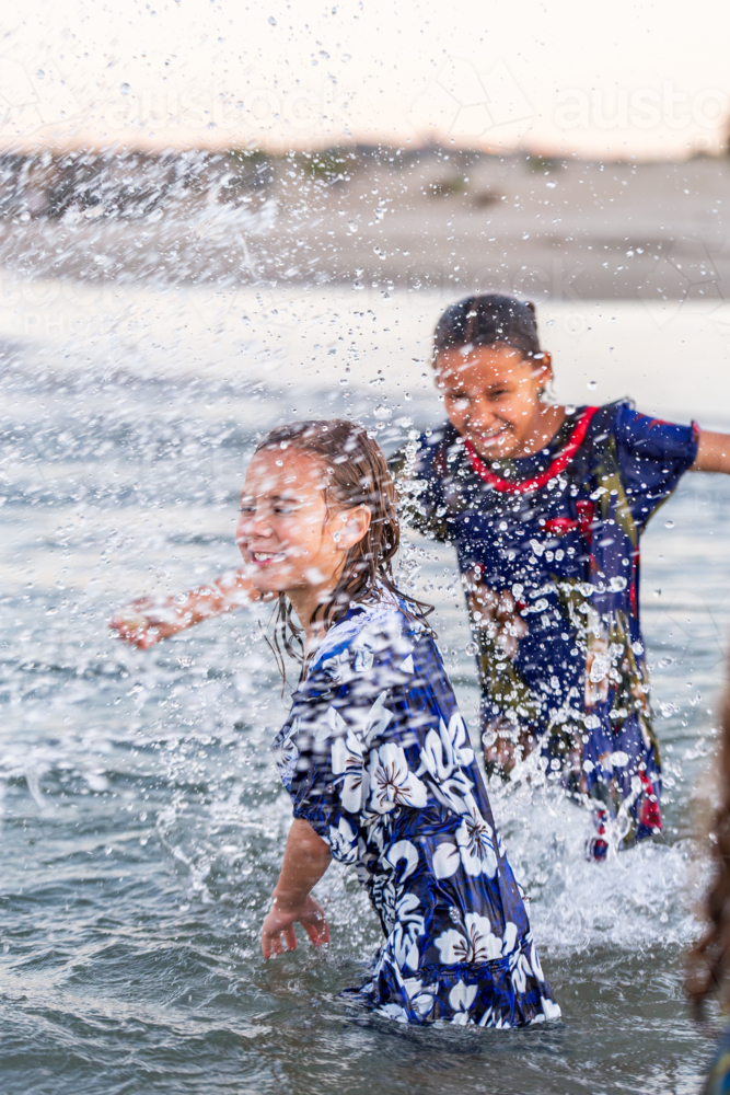 Image of Torres Strait Islander girls in traditional floral dresses playing and splashing in ...