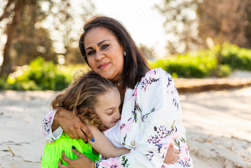 Image of Torres Strait Islander mother in her thirties and young daughter hug together on beach ...