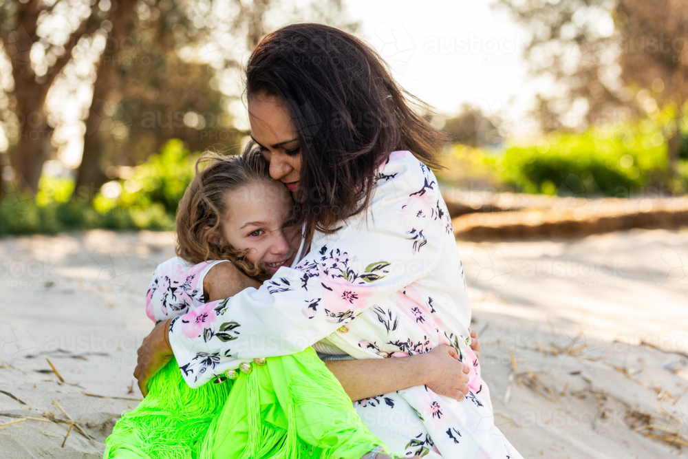 Image of Torres Strait Islander mother in her thirties and young daughter hug together on the ...