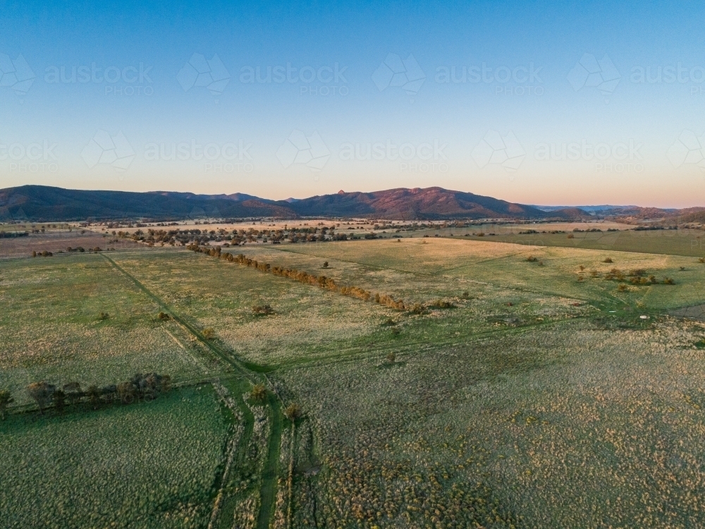 Image of Track through pastoral farm paddock at sunset seen from drone ...