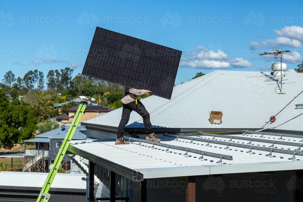 Image of Tradesman carrying solar panel onto metal roof of suburban ...