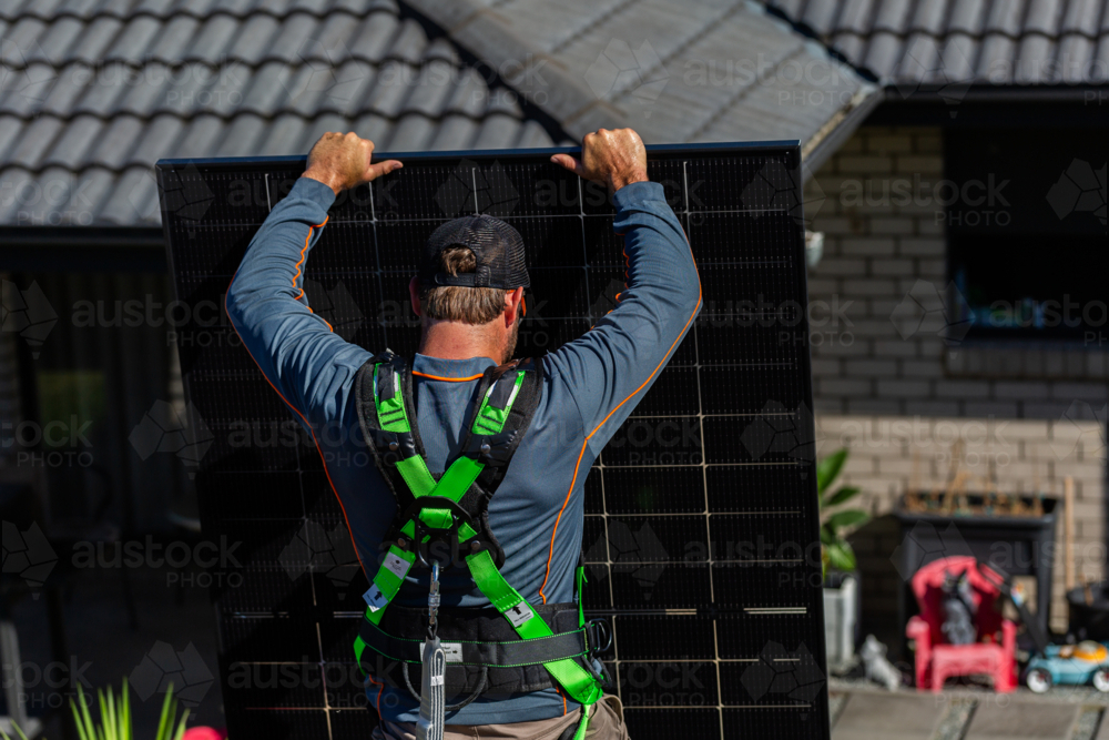 Image of Tradesman electrician lifting black bi-facial solar panels ...