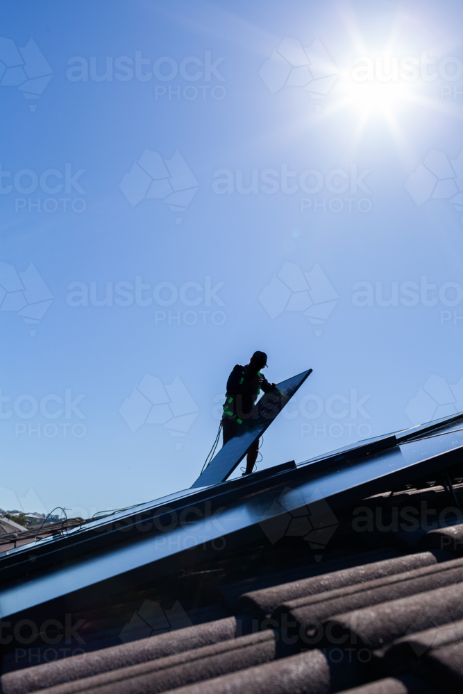 Image of Tradie man laying solar panel on roof under blue sky during ...