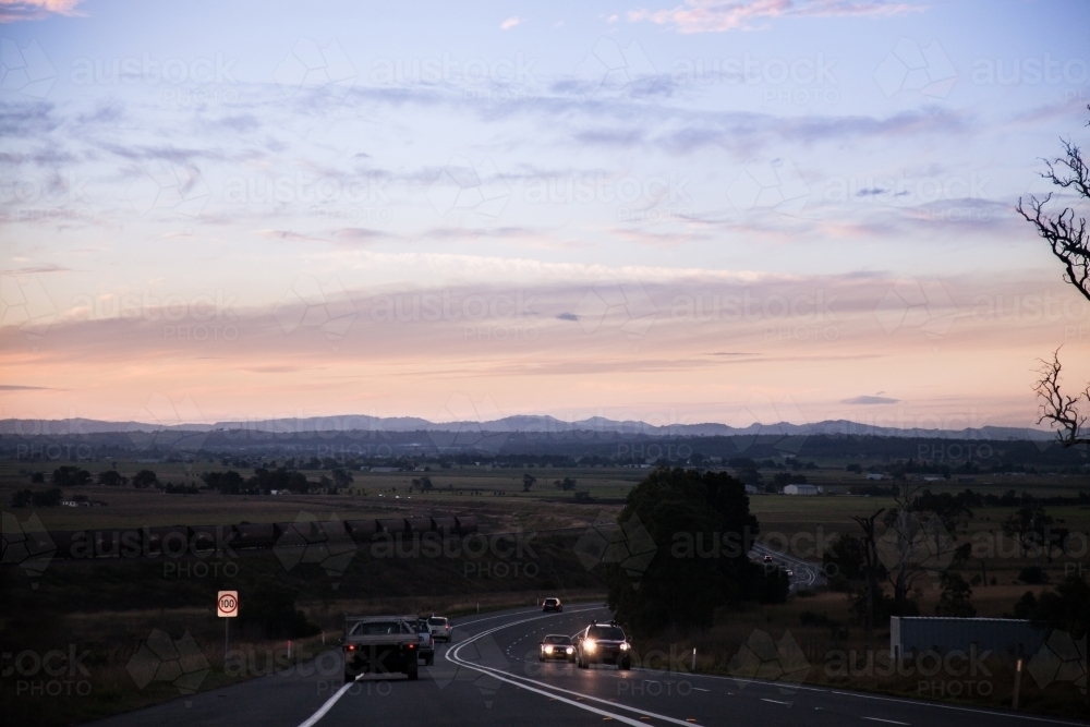 Image of Traffic driving on road at dusk - Austockphoto
