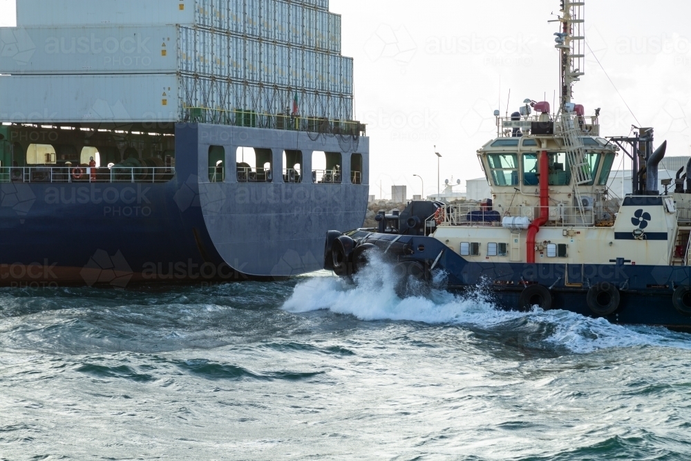 Image of Tug boat following a blue hulled container ship. - Austockphoto