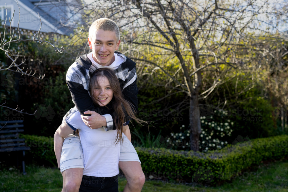 Image of Tween girl carrying teen brother on her back - Austockphoto