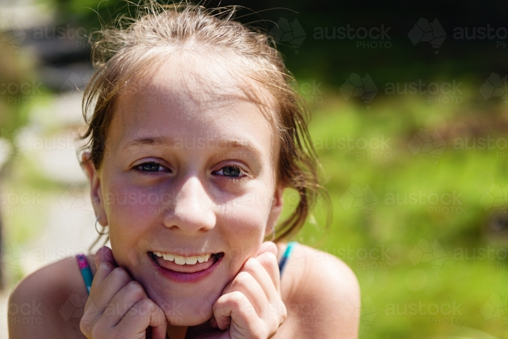 Image of Tween girl smiling with her hands on her chin under the sun ...