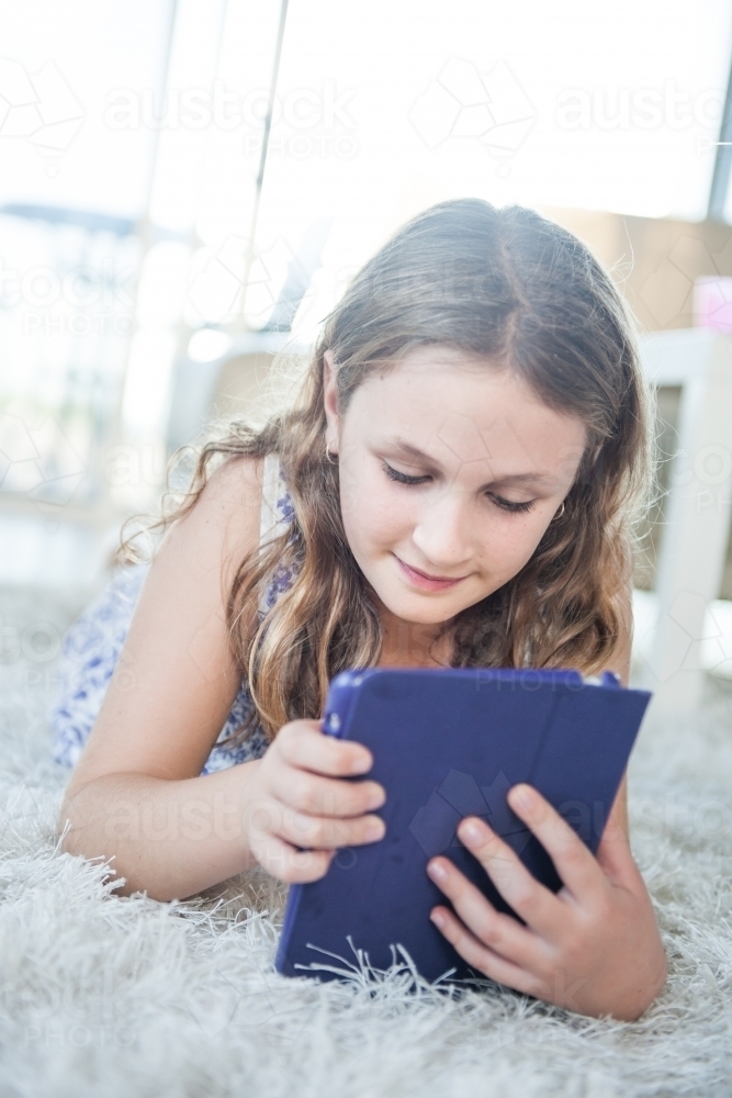 Image of Tween girl using iPad whilst lying the floor on a white rug ...