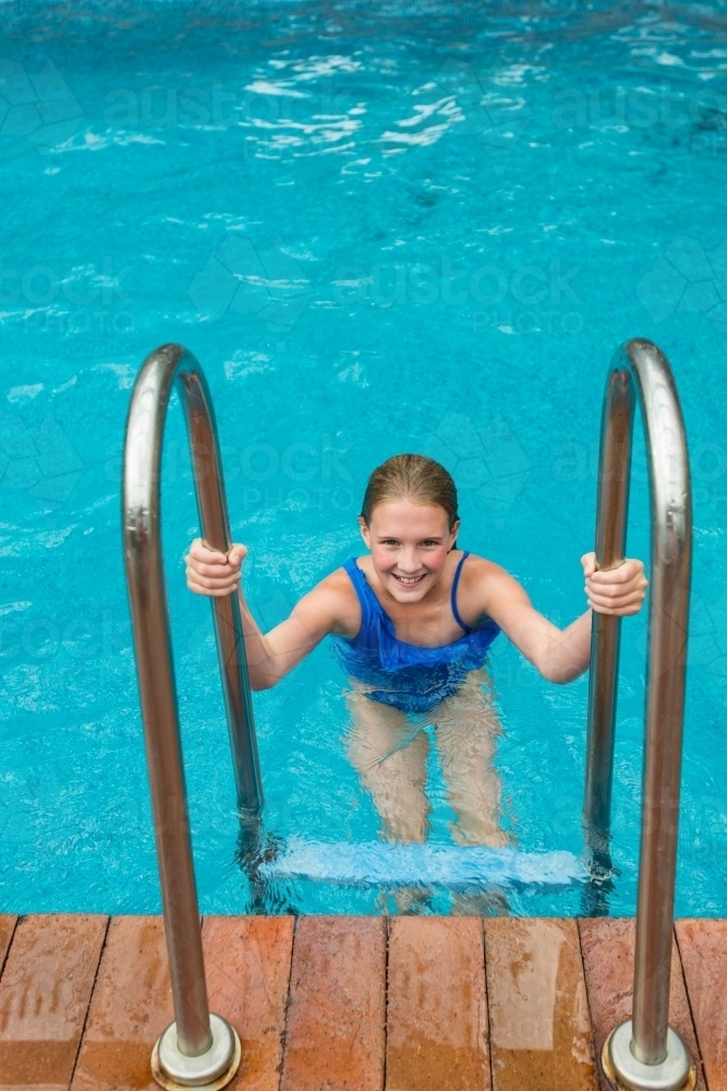 Image of tween girl using ladder to exit pool - Austockphoto