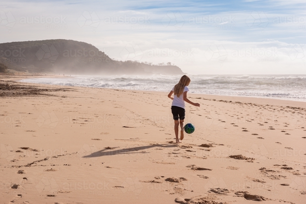 Image of Tween girl with a ball running along sandy beach - Austockphoto