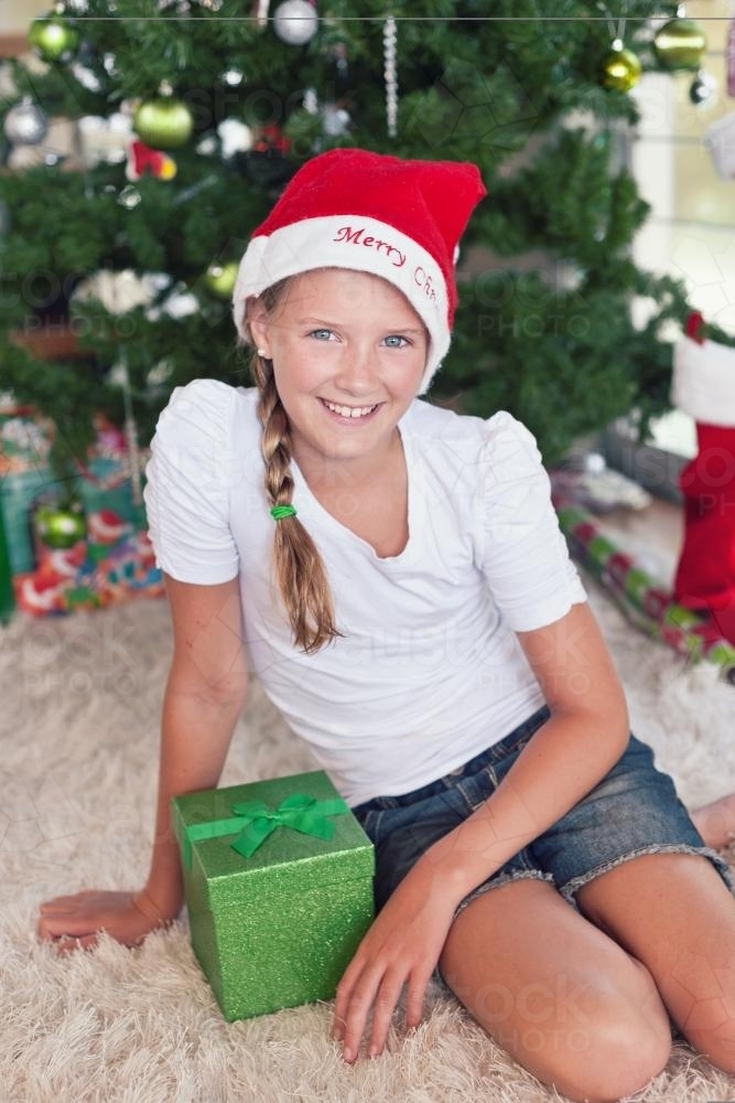 Image of tween girl with xmas present in front of xmas tree - Austockphoto