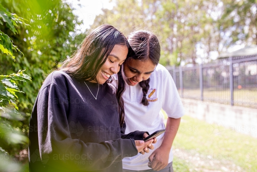 Image of Two Aboriginal girls talking and looking at a phone - Austockphoto