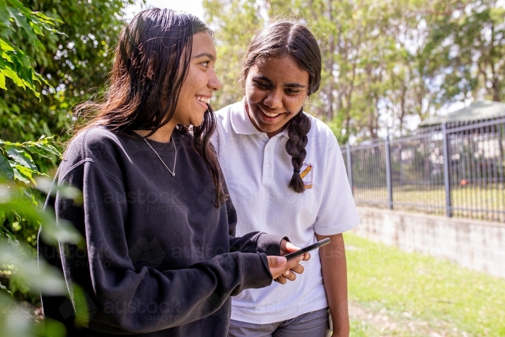 Image of Two Aboriginal girls talking and looking at a phone - Austockphoto