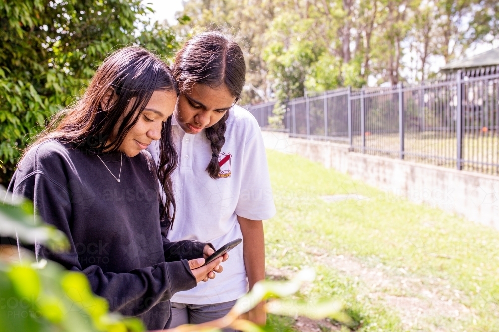 Image of Two Aboriginal girls talking and looking at a phone - Austockphoto