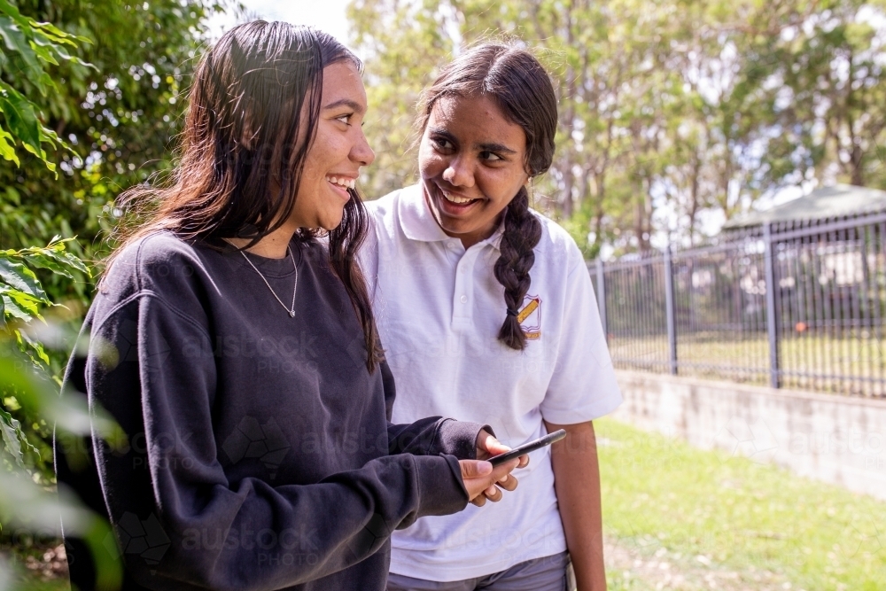 Image of Two Aboriginal girls talking and looking at a phone - Austockphoto