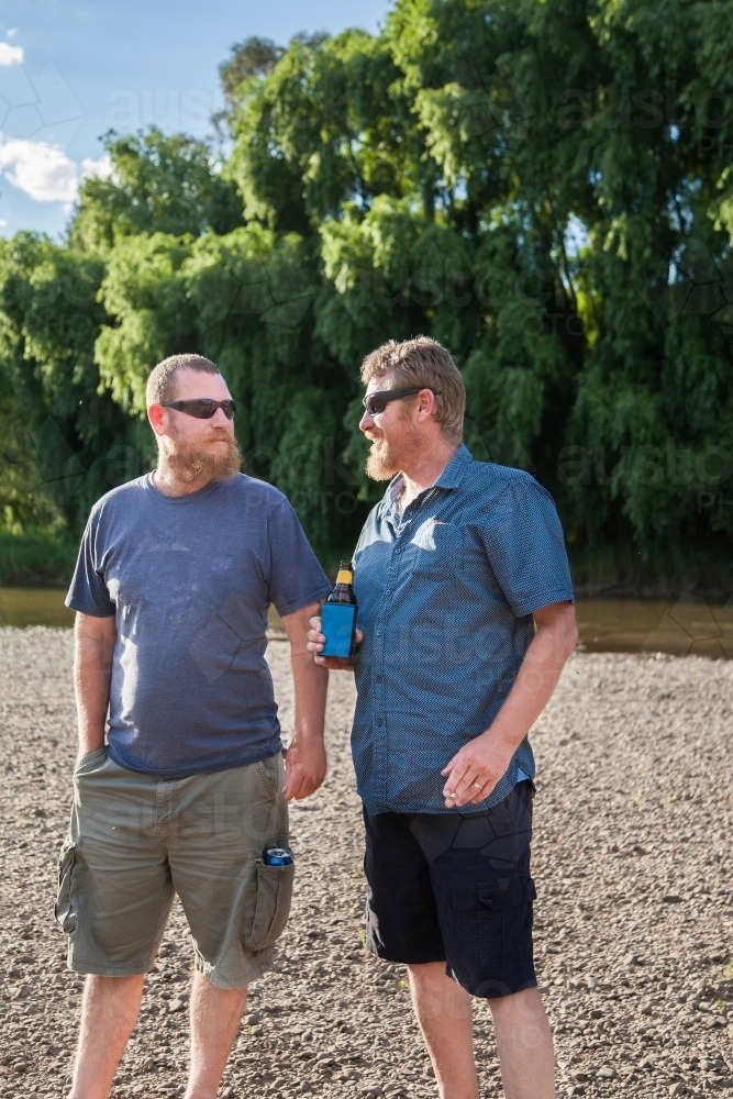 Image of Two blokes drinking a beer together by the river - Austockphoto