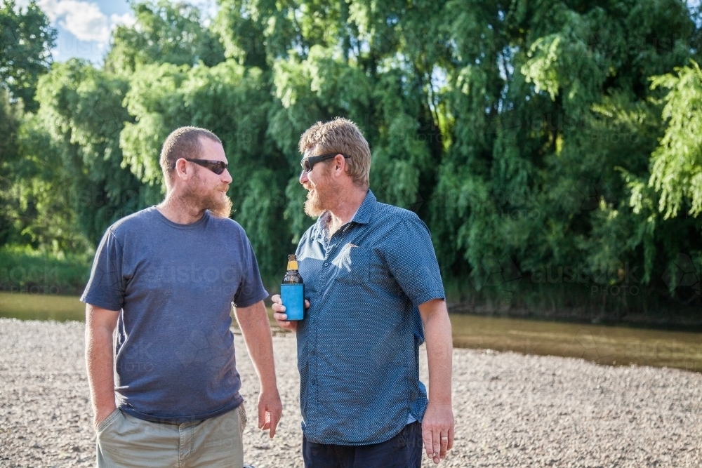 Image of Two blokes drinking a beer together by the river - Austockphoto