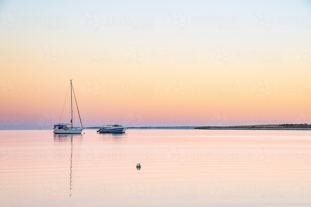 Image of Two boats sailing on calm water at dawn in the bay. - Austockphoto