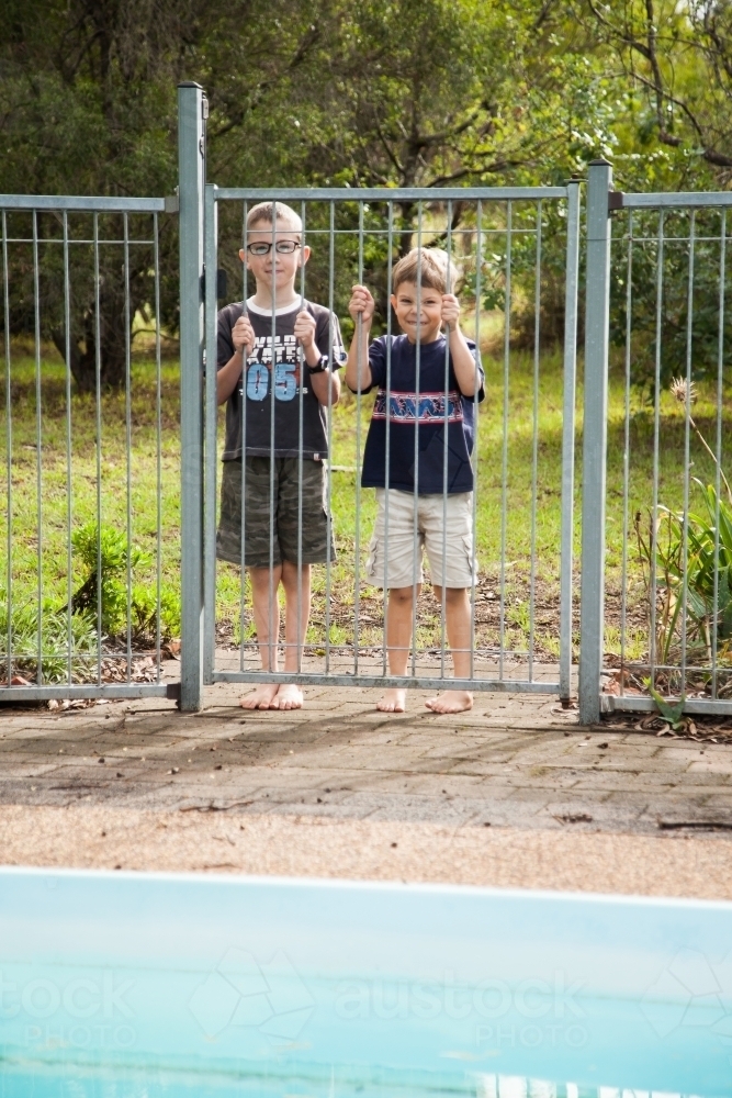 Image of Two boys standing outside pool fence gate holding bars ...