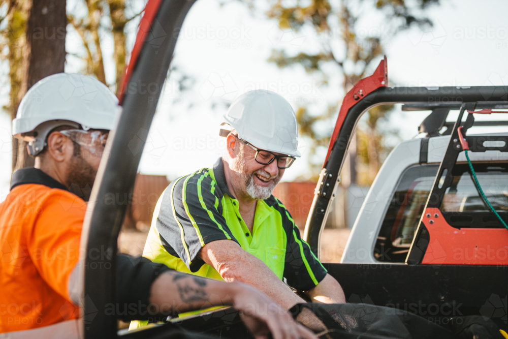 Image of Two builders standing next to the ute laughing together ...