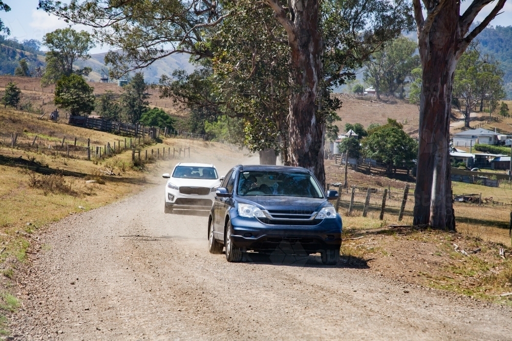 Image of Two cars driving on narrow gravel road in country - Austockphoto