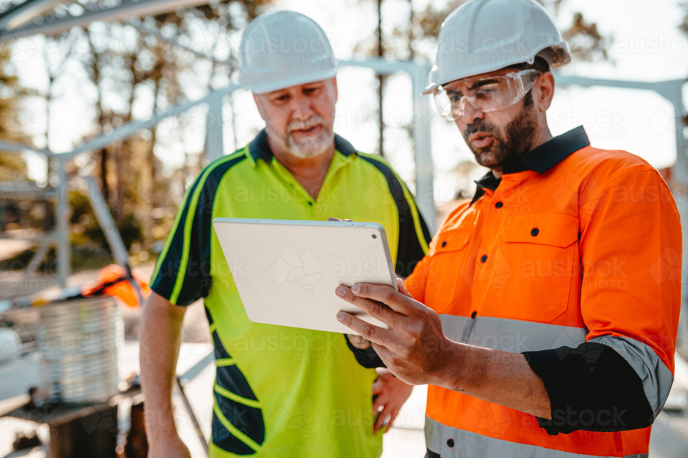 Image of Two construction site managers looking at digital blueprints ...