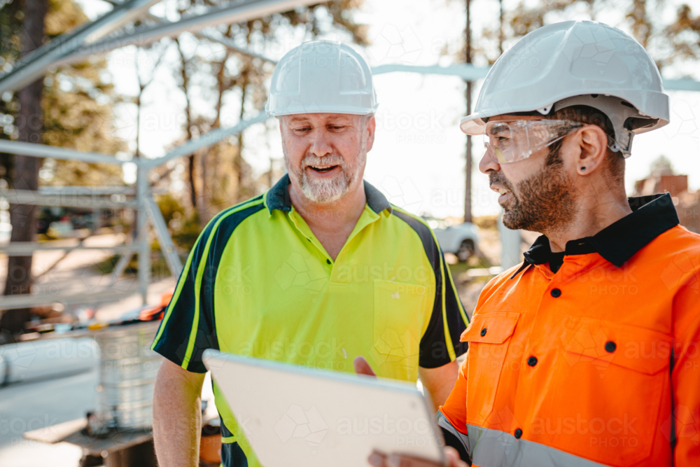 Image of Two construction workers in hardhats looking at digital ...