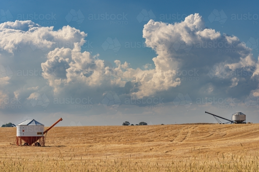 Image of Two field bins sitting in a paddock under a dark cloudy sky ...