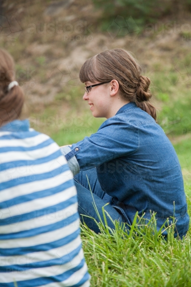 Image of Two friends sitting on the grass talking - Austockphoto