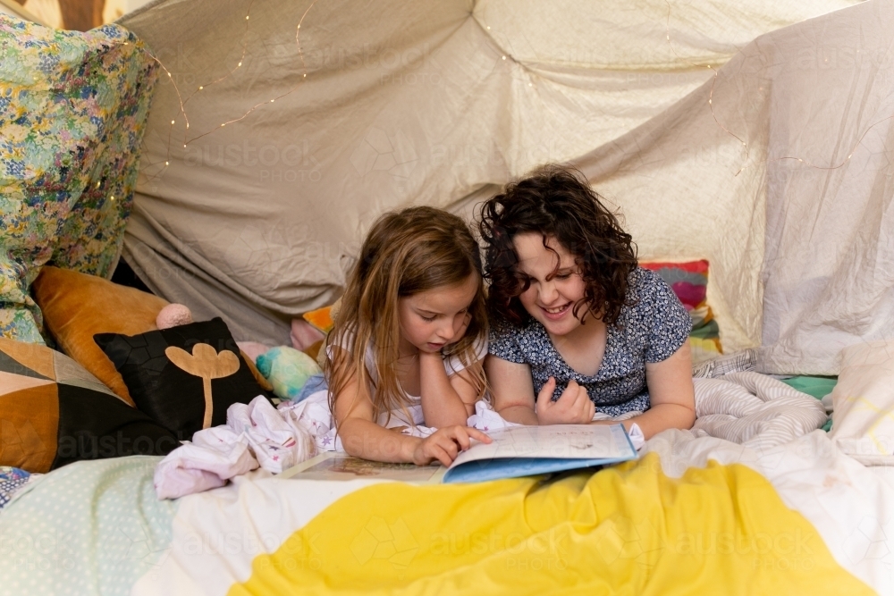 Image of Two happy girls reading a book together in cubby house tent ...