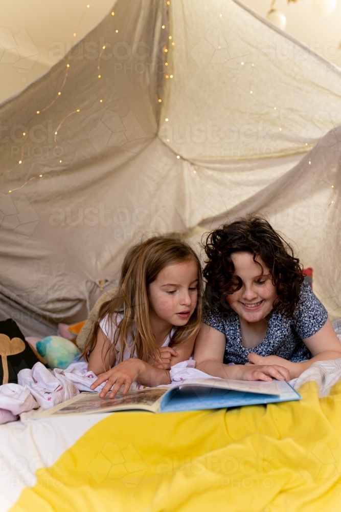 Image of Two happy girls reading a book together in cubby house tent ...