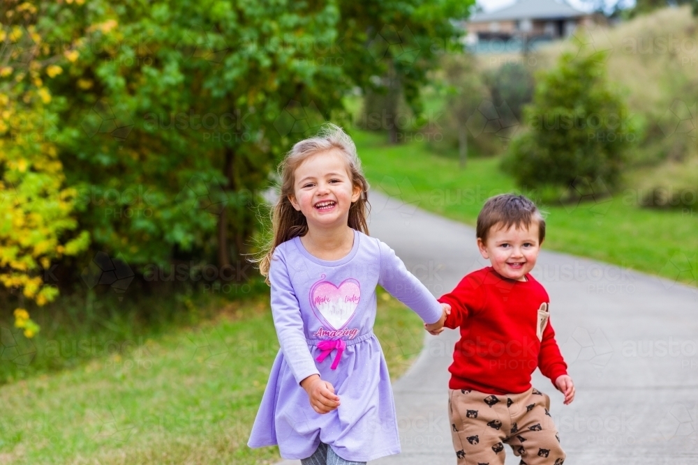 Image of Two happy children running together along a footpath outside ...