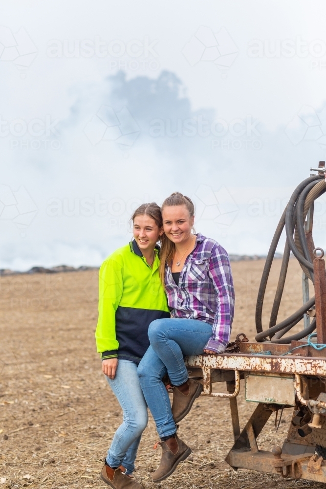 Image of Two happy country girls sitting on back of ute with smoky ...