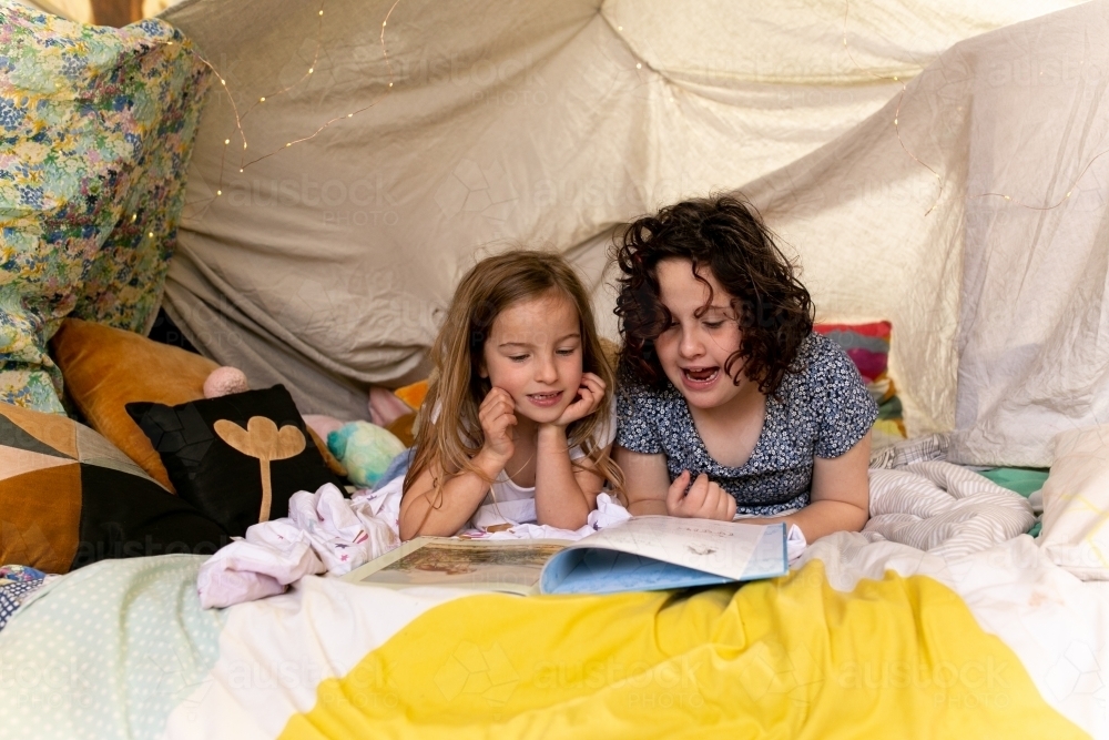 Image of Two happy girls reading a book together in cubby house tent ...