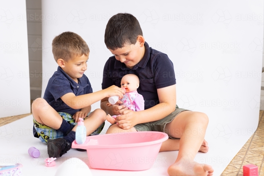 Image of Two little boys playing with a baby doll - Austockphoto