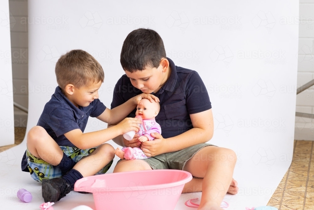 Image of Two little boys playing with a baby doll - Austockphoto