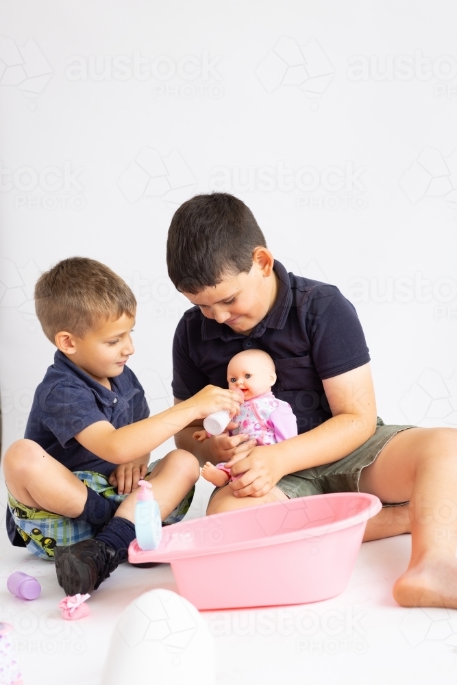 Image of two little boys playing with a baby doll on plain white ...