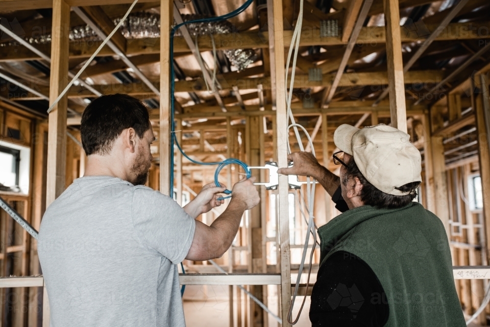 Image of two men are laying cables in a house at frame stage - Austockphoto