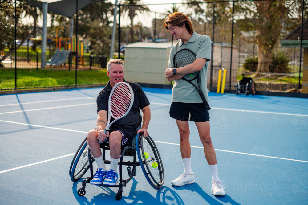 Image of Two men interact on a tennis court, with one in a wheelchair ...